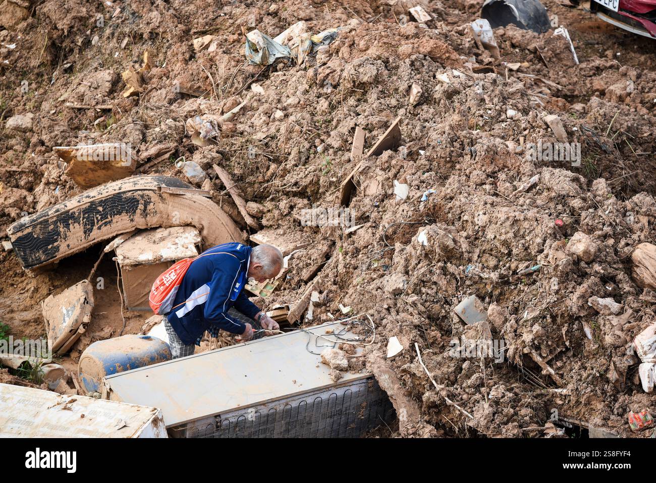 Man repairing an abandoned fridge in the middle of debris and soil pile ...