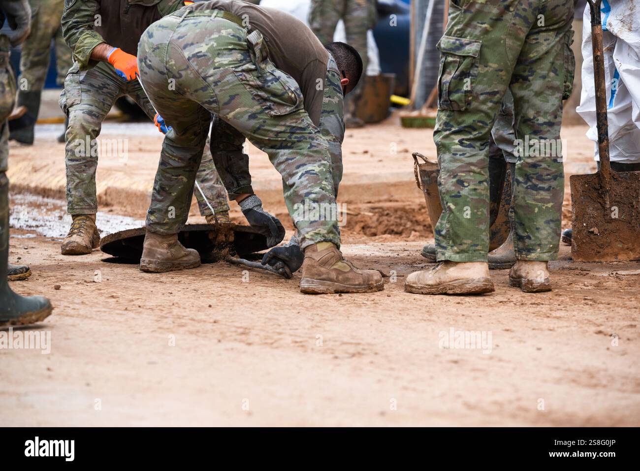 Military Army members open a stuck manhole cover in a muddy street ...