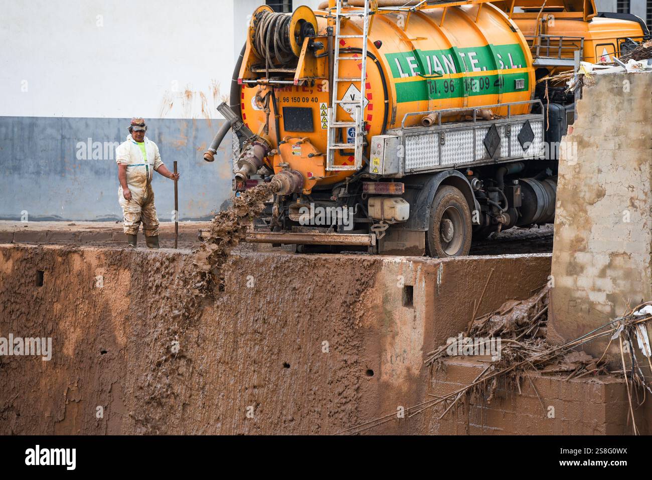 Worker in white coverall and sewer dredge cleaning truck throwing mud ...