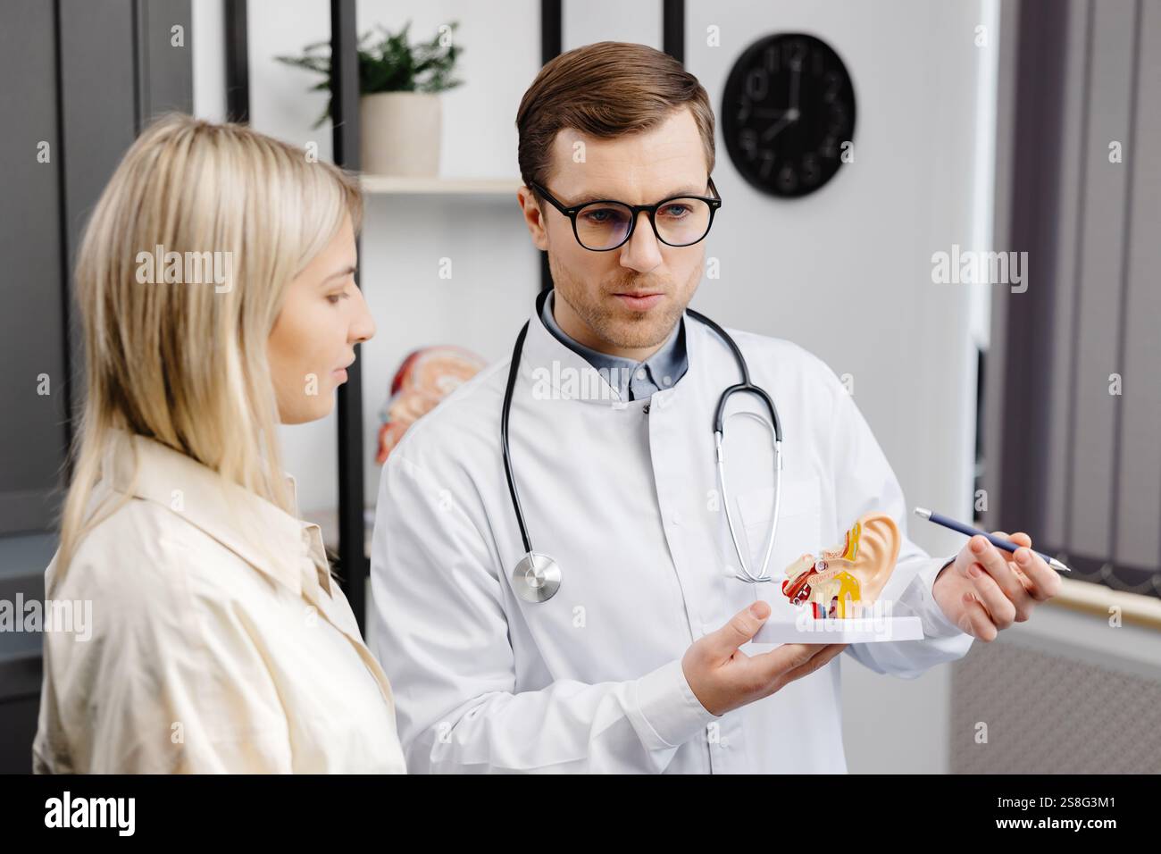 A young attractive otolaryngologist doctor shows a model of the ear and ...