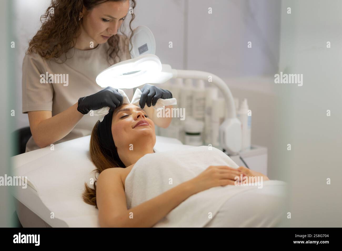 A woman enjoys a rejuvenating facial treatment at a tranquil spa. A skilled aesthetician gently ...