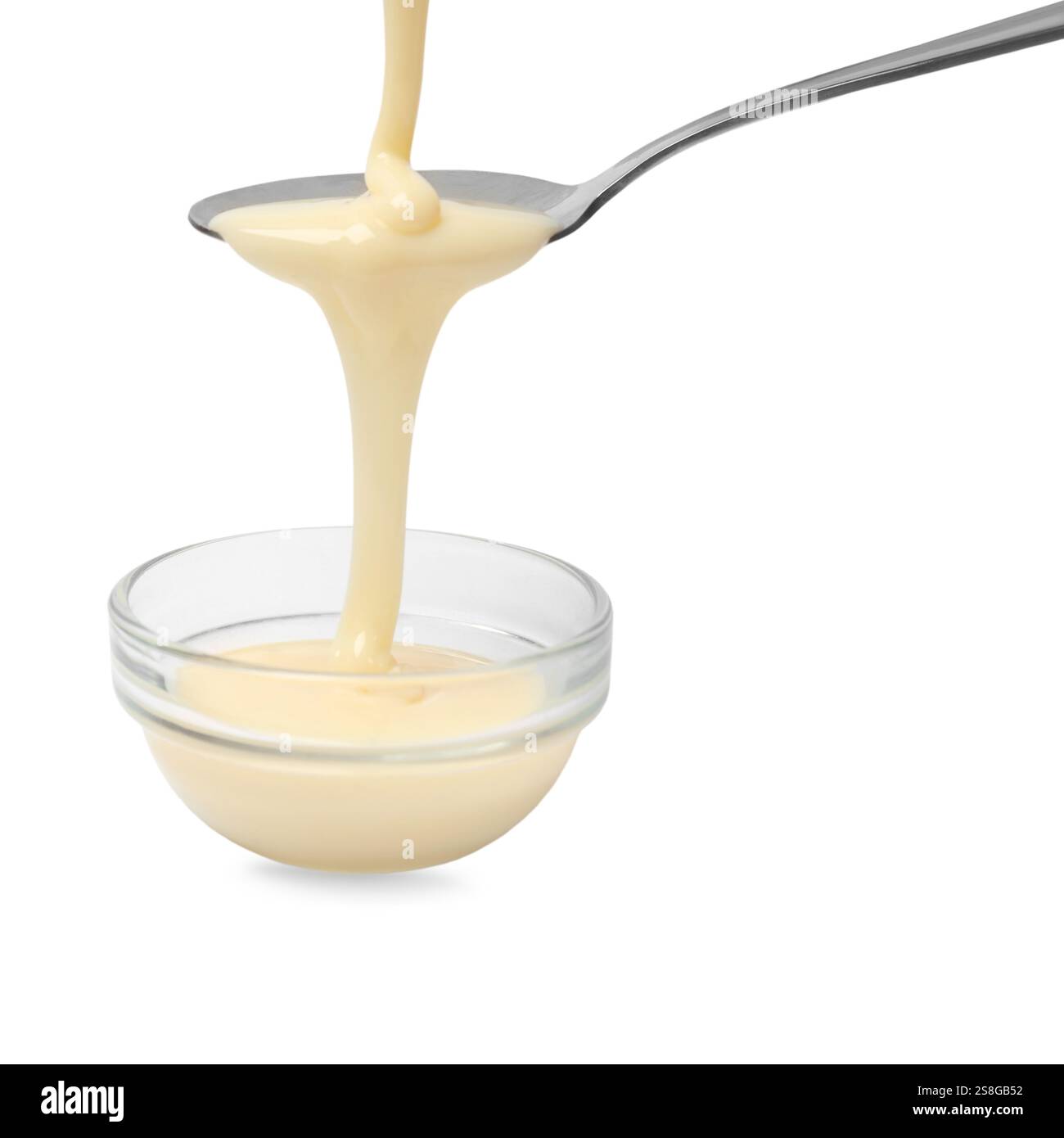 Condensed milk flowing down from spoon into bowl isolated on white ...