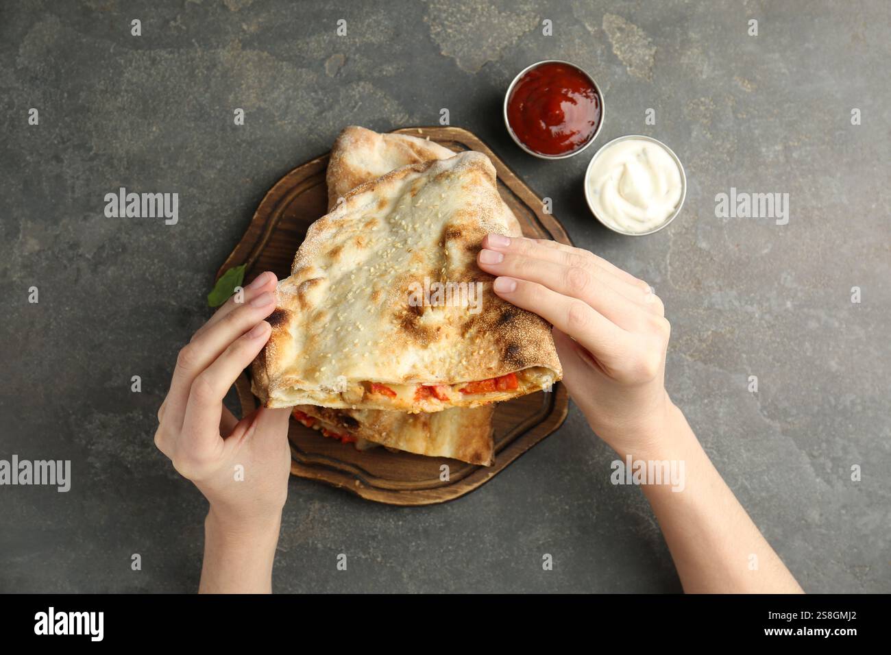 Woman eating tasty calzone with meat, cheese and tomato at grey ...
