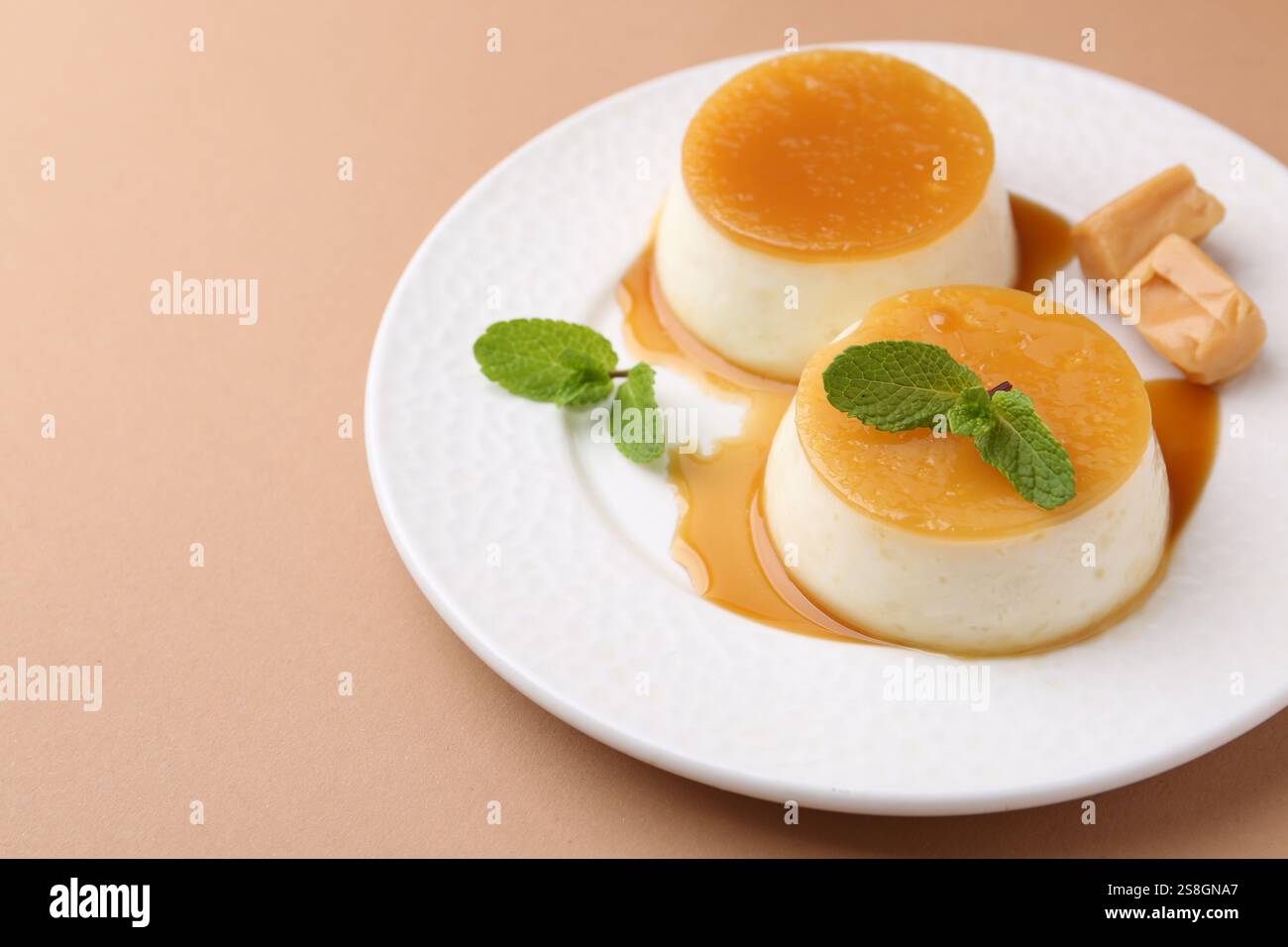 Tasty puddings with caramel sauce served on light brown background ...