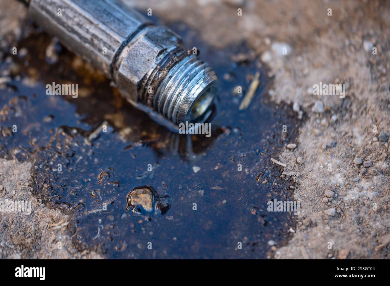 A pipe is dripping oil onto the ground. The water is brown and the pipe ...