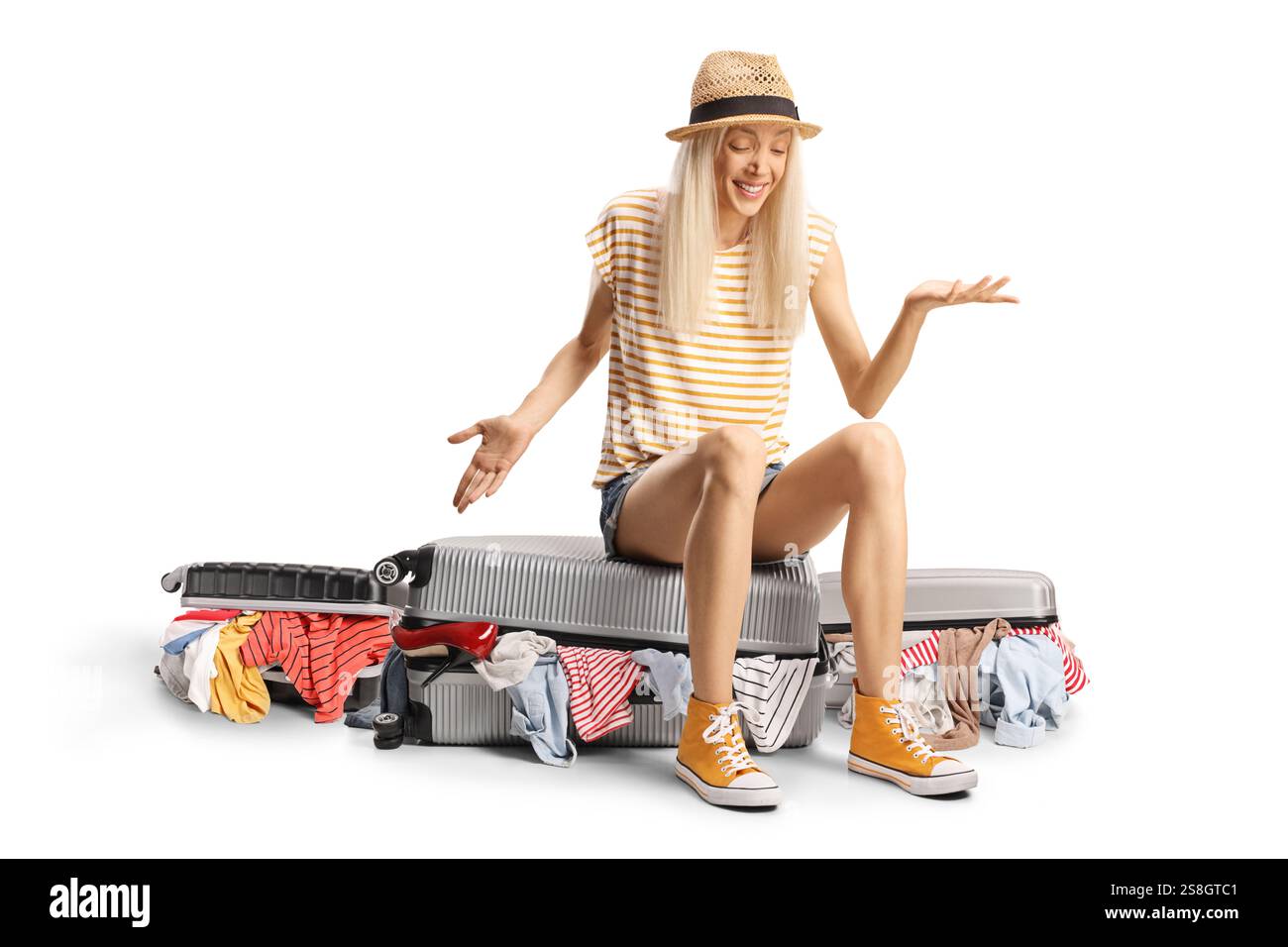 Young woman sitting on overpacked suitcases and laughing isolated on ...