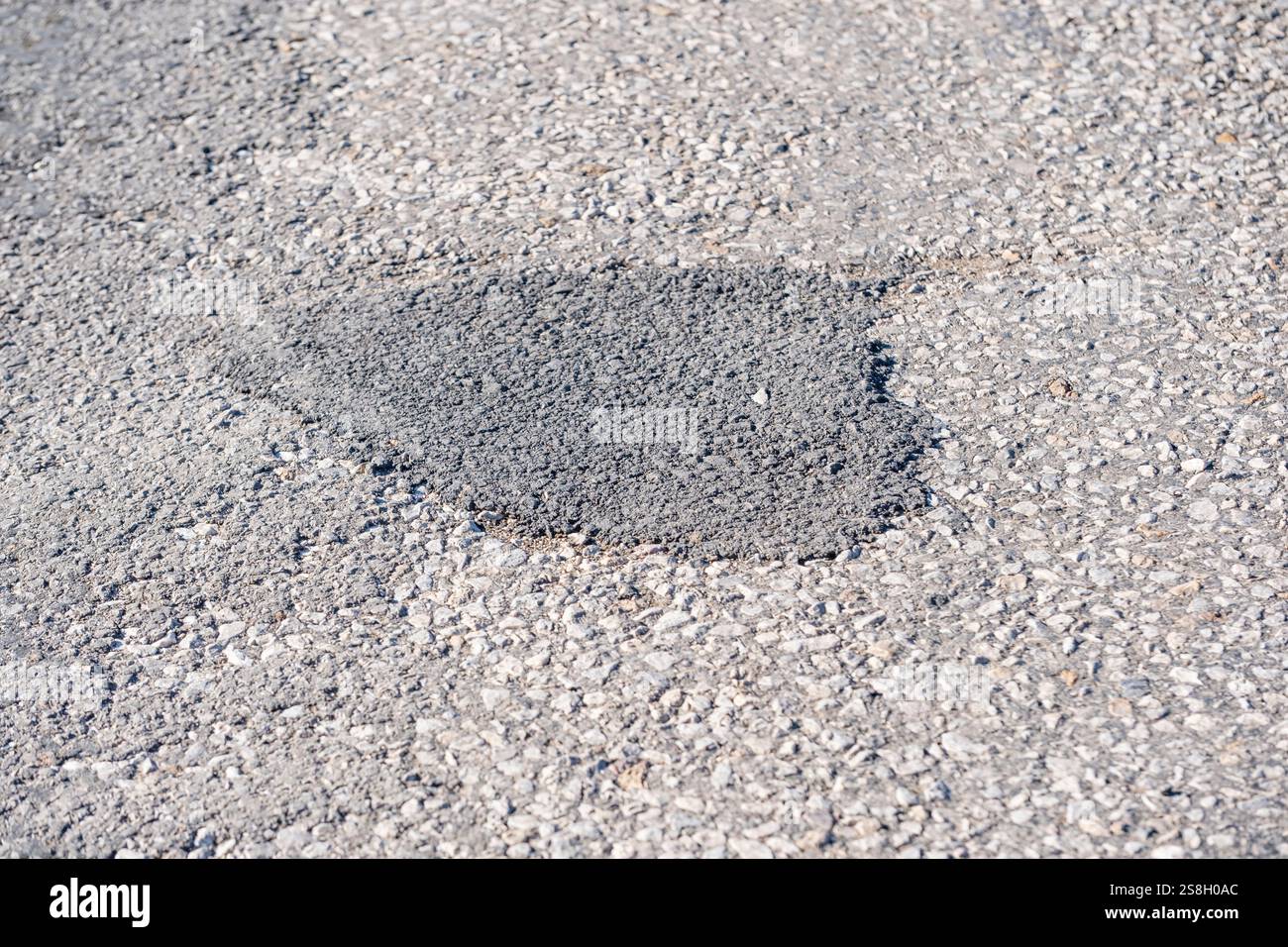 A pothole in the road with gravel and rocks. The pothole is small and ...