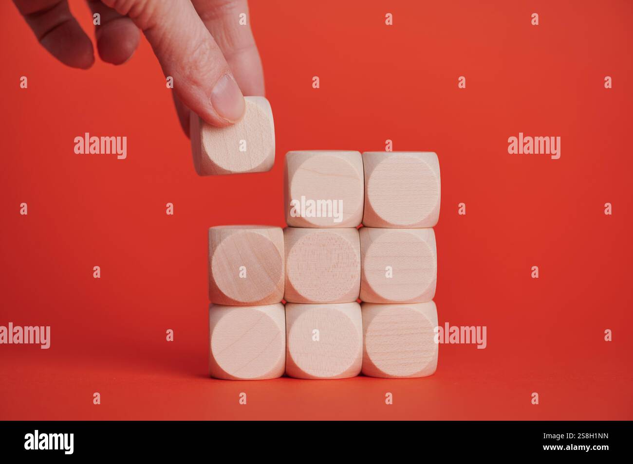Hand places a wooden block atop a stacked arrangement of blocks on a ...