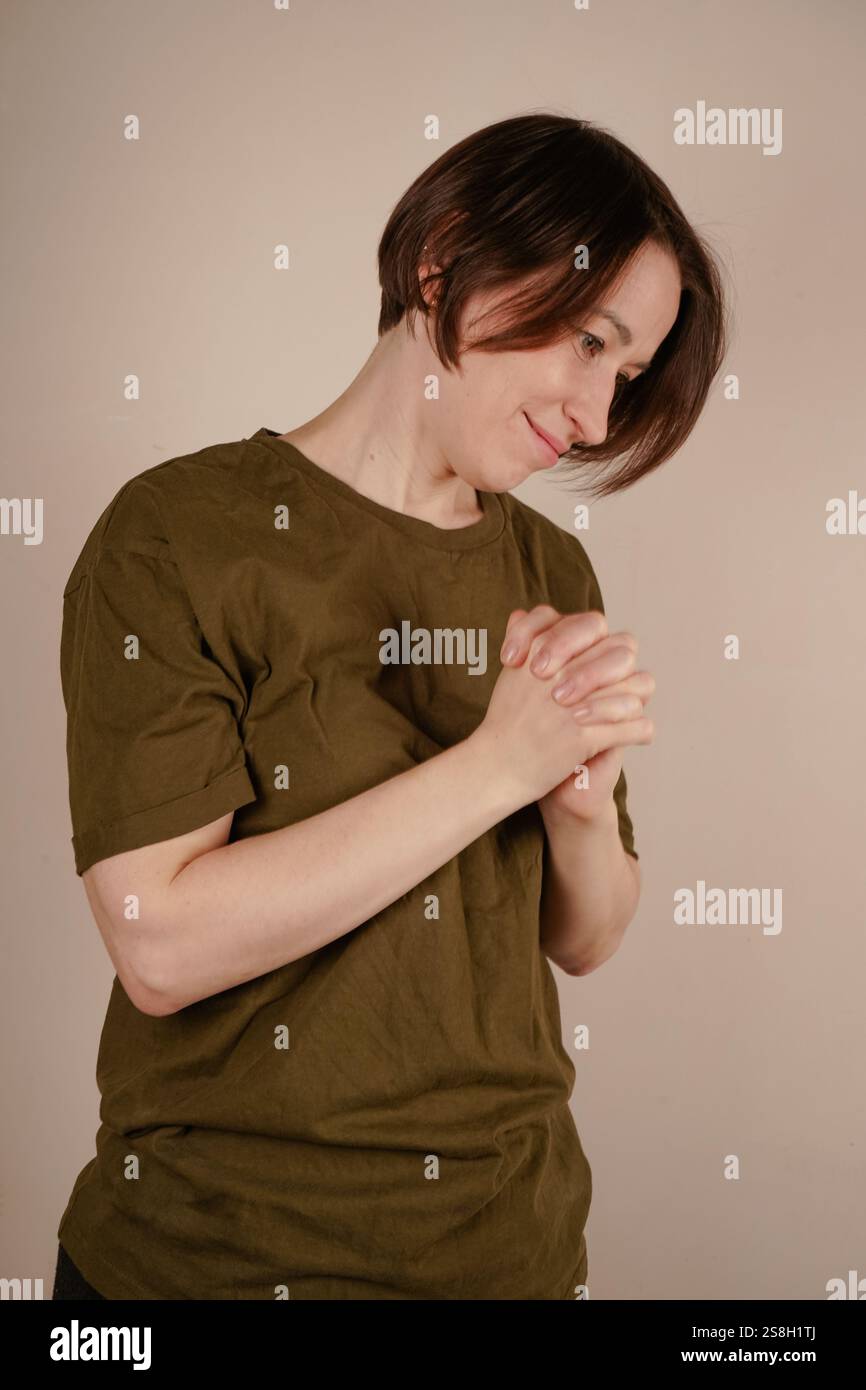 Photo of hopeful beautiful woman with dark hair holding hands together ...