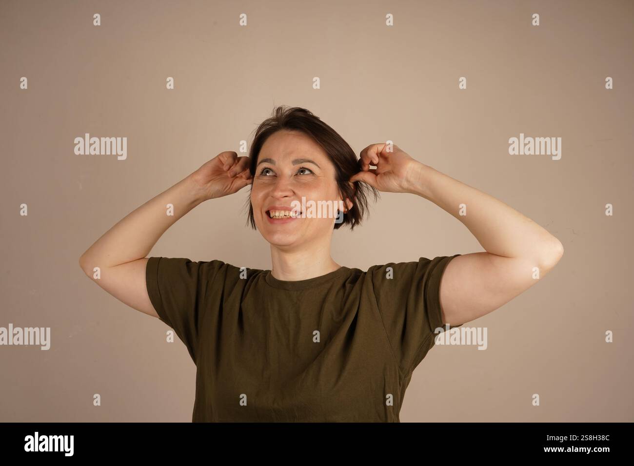 Portrait of a young happy woman touching her ear on gray background ...