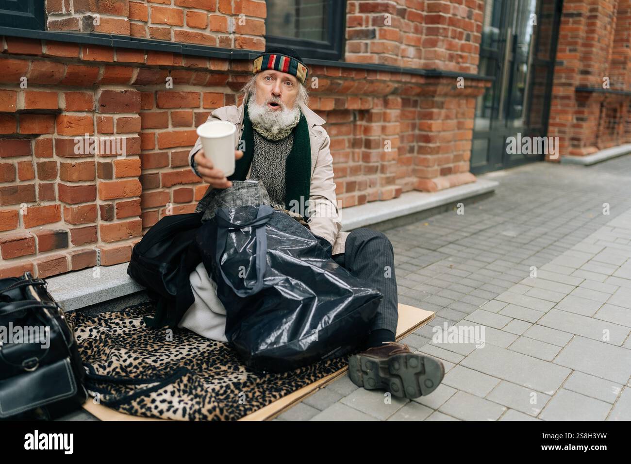 Portrait of angry older homeless man sitting on urban street with ...