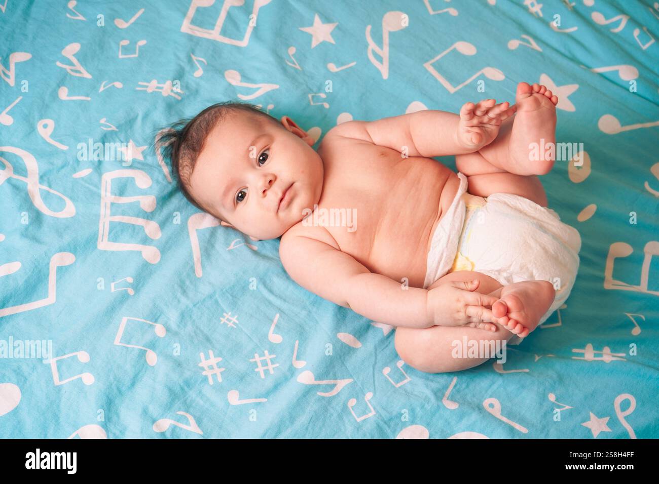 Lying on its back, the baby stares at the ceiling with wide, fascinated ...
