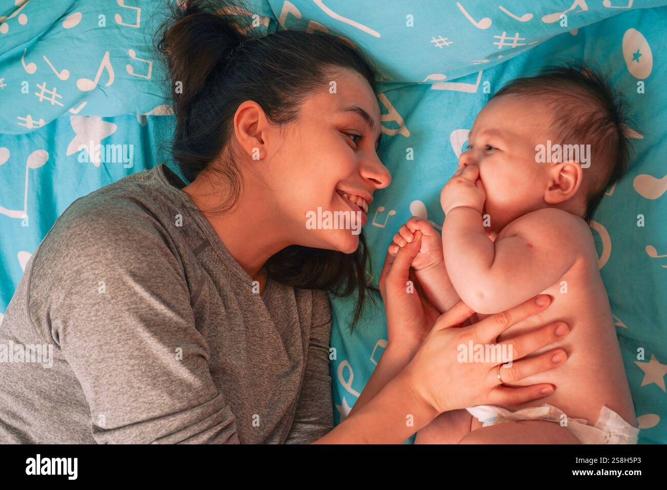 Happy mom lies peacefully on bed, hugging and cuddling her newborn baby ...