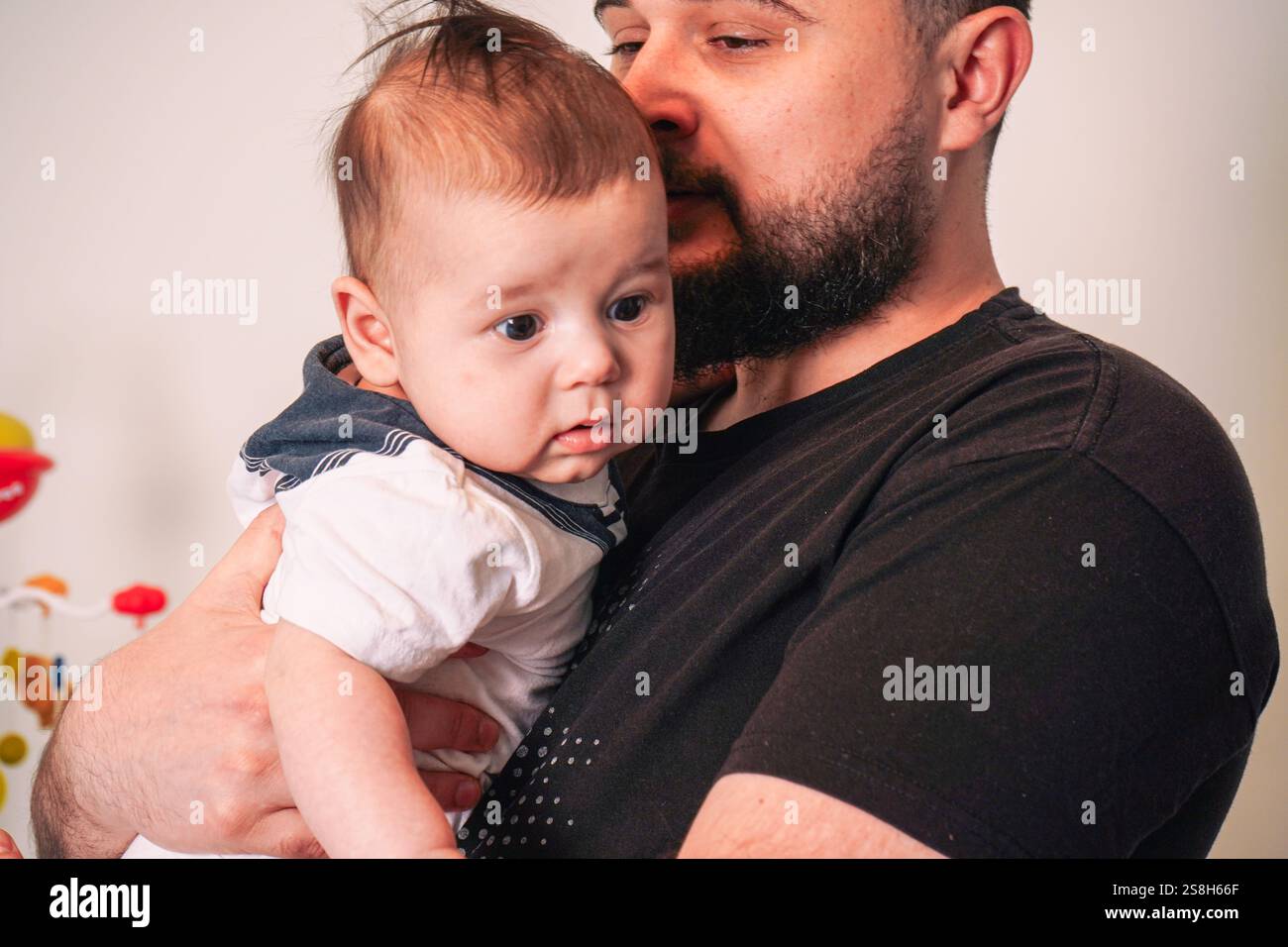 The father cradles the baby close, his arms wrapping protectively ...