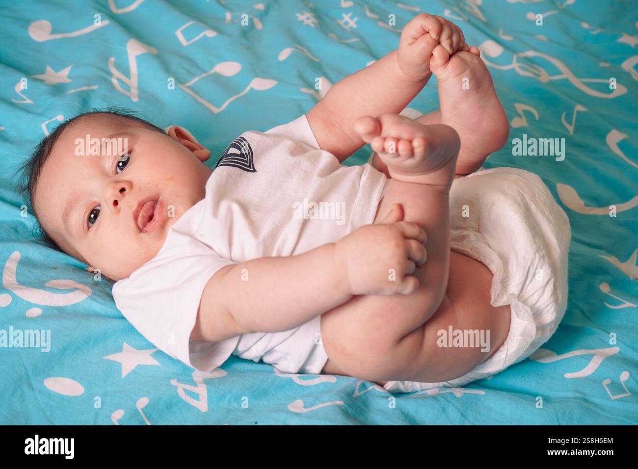 The baby's delicate fingers curl slightly as he reaches for his legs ...