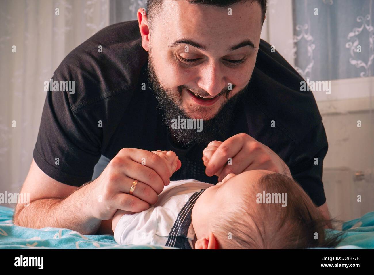 The baby in a white onesie giggles, bringing a warm smile to the father ...