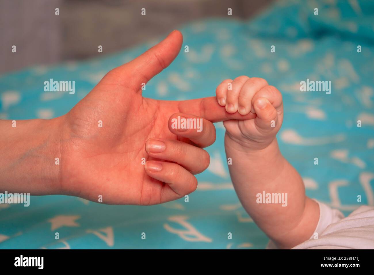A close-up captures the tiny hand of a baby holding onto a parent's ...