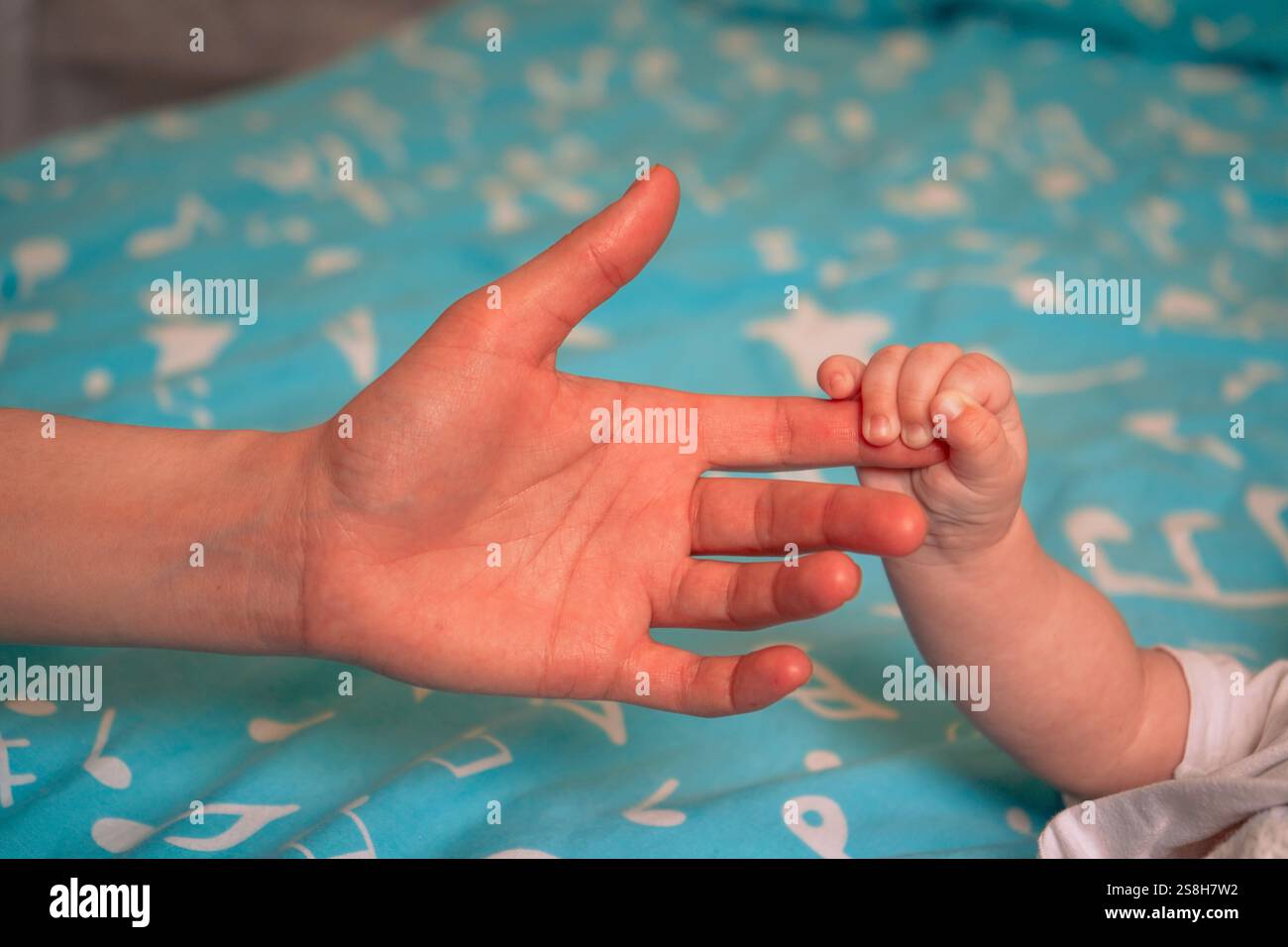 Tiny fingers curl around the parent's finger, embodying the innocence ...