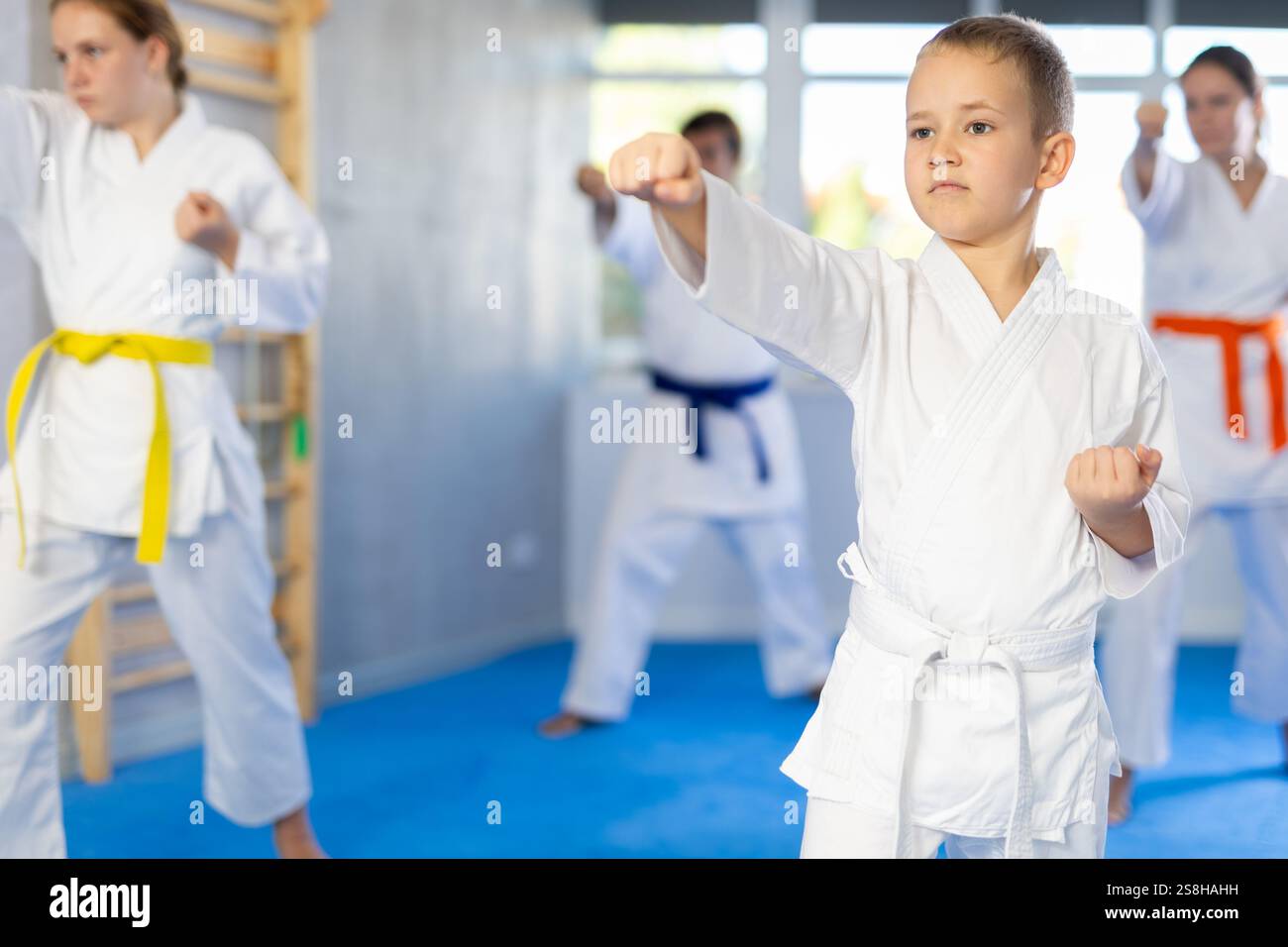 Boy in kimono performing punch moves in gym during group training with ...