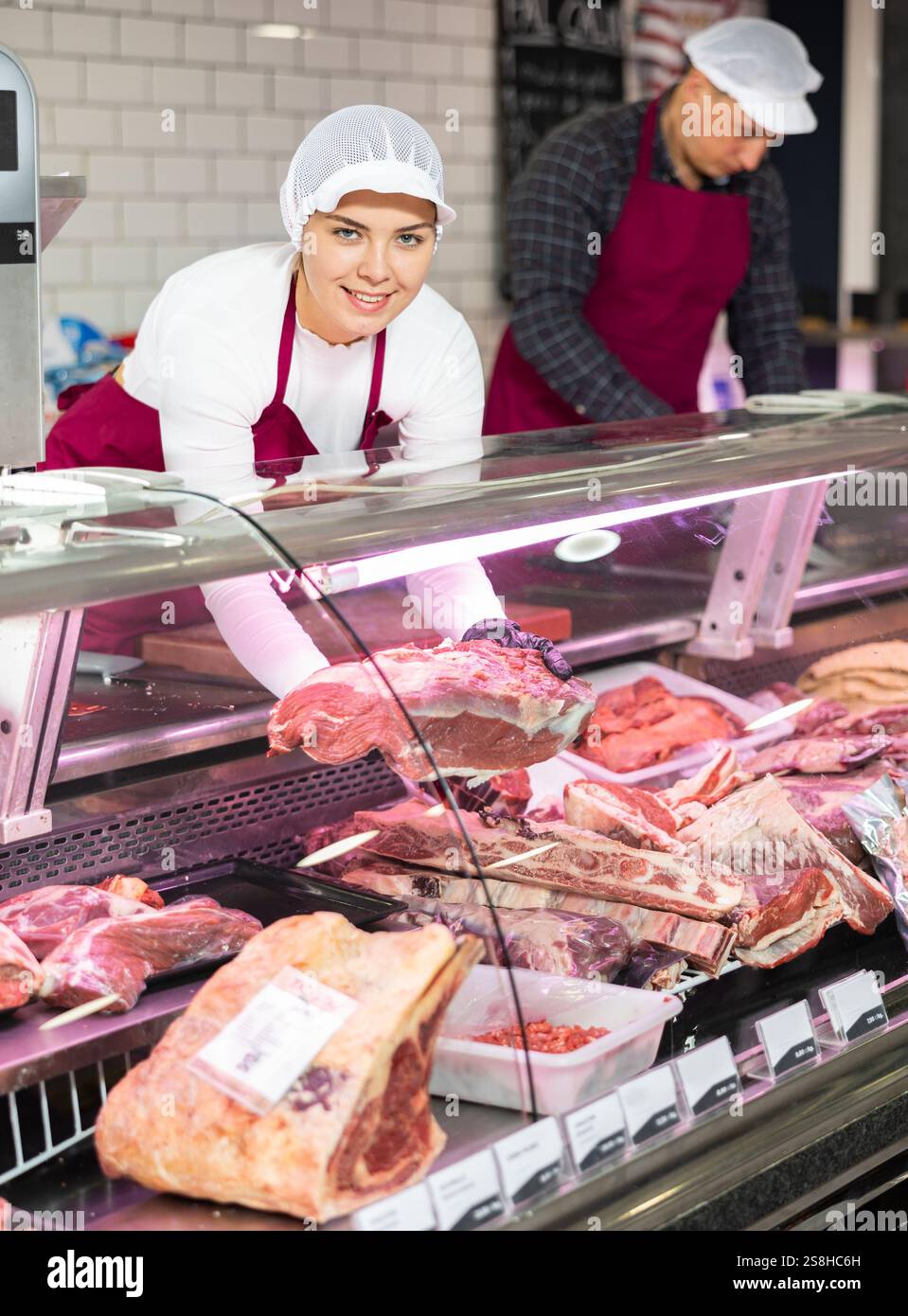Happy female butcher holding big chunk of beef meat in meat section of ...