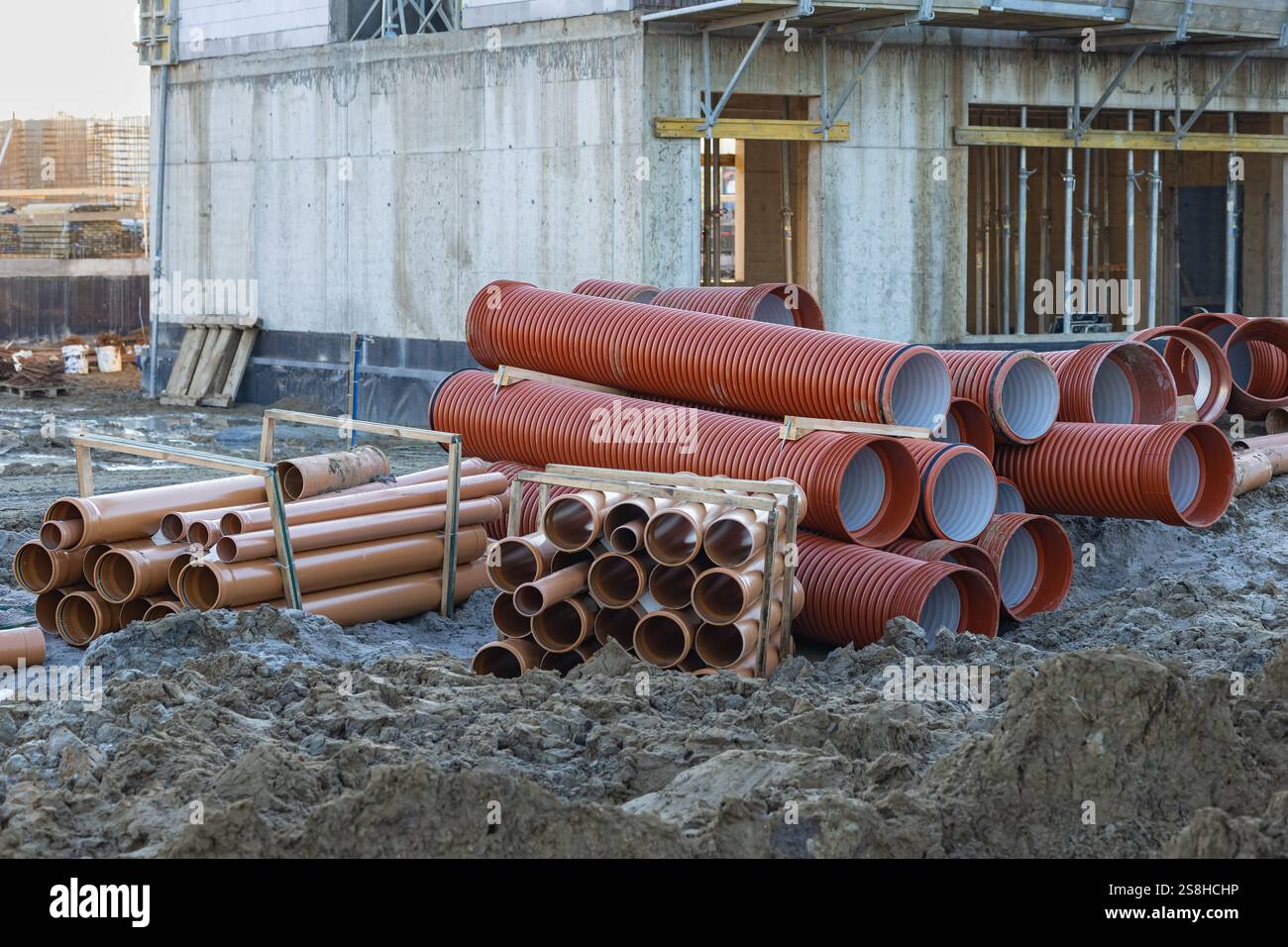Stacks of construction pipes on a building site with muddy ground and ...