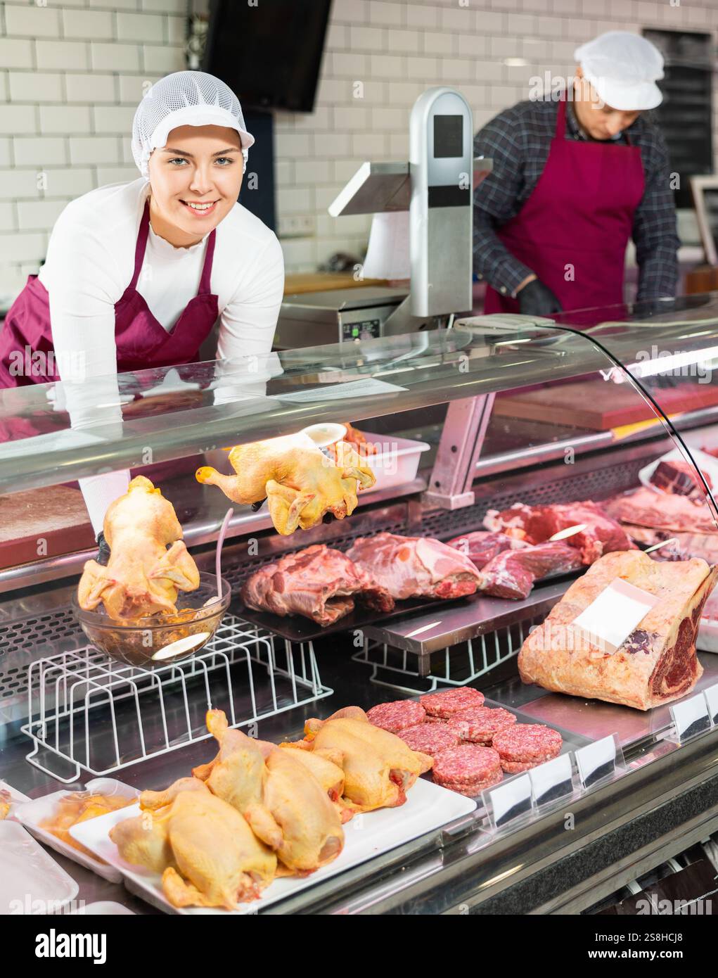 Happy female butcher holding whole chicken in meat section of ...