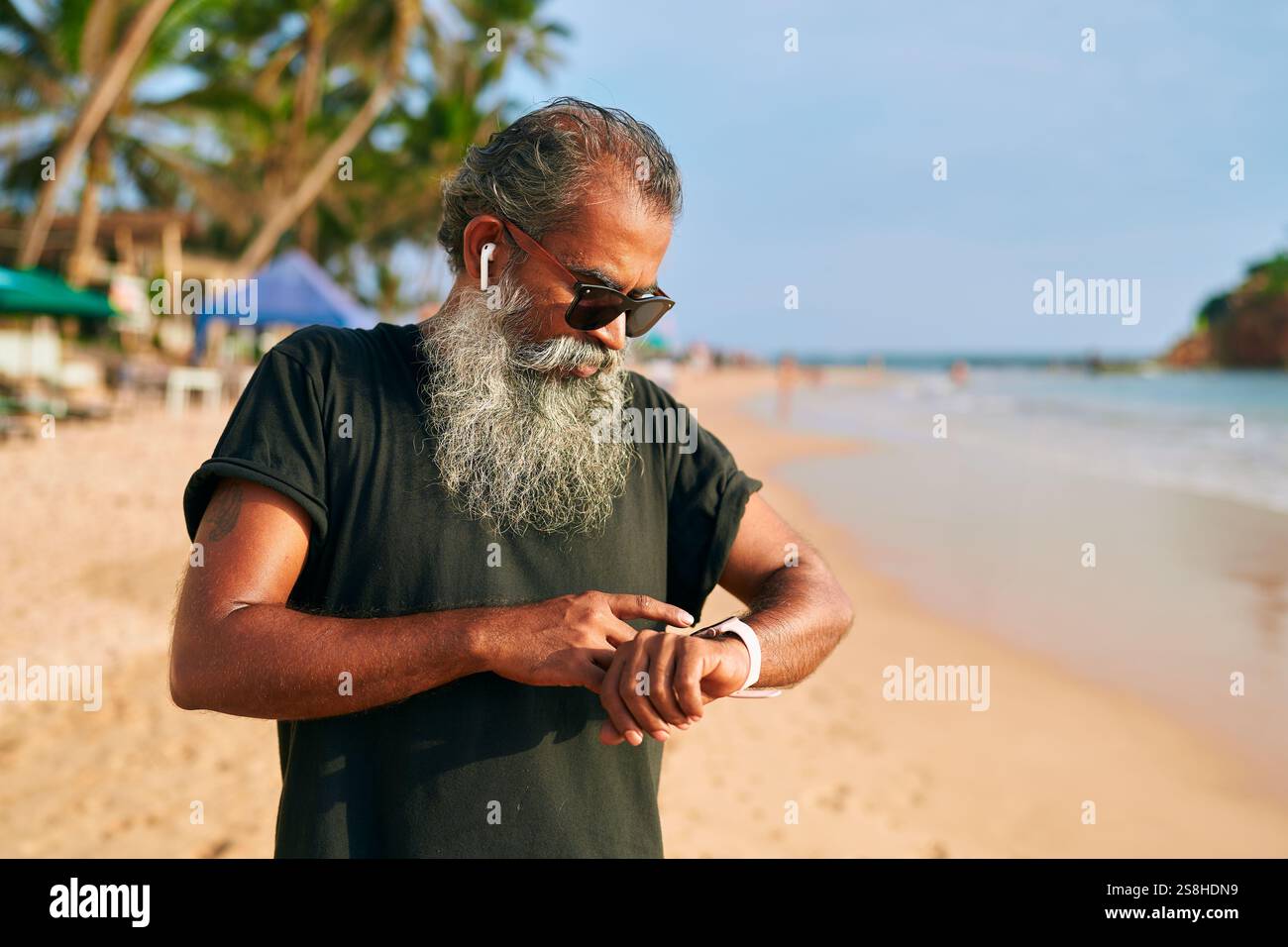 Senior stylish man with gray beard on beach uses smart watch gadget ...