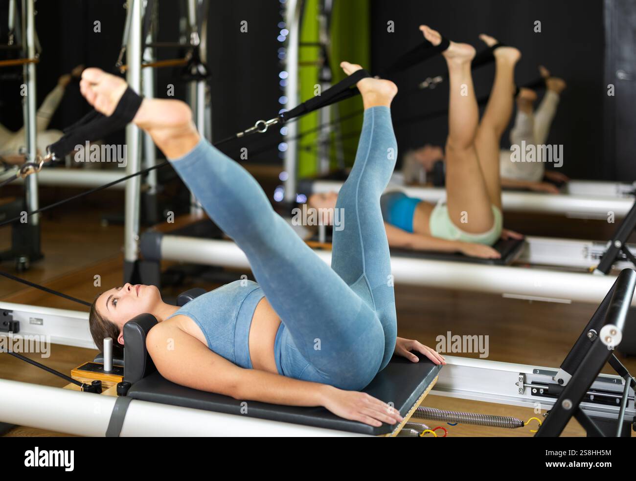 Woman lying on reformer and pulling adjustable cables with her legs ...