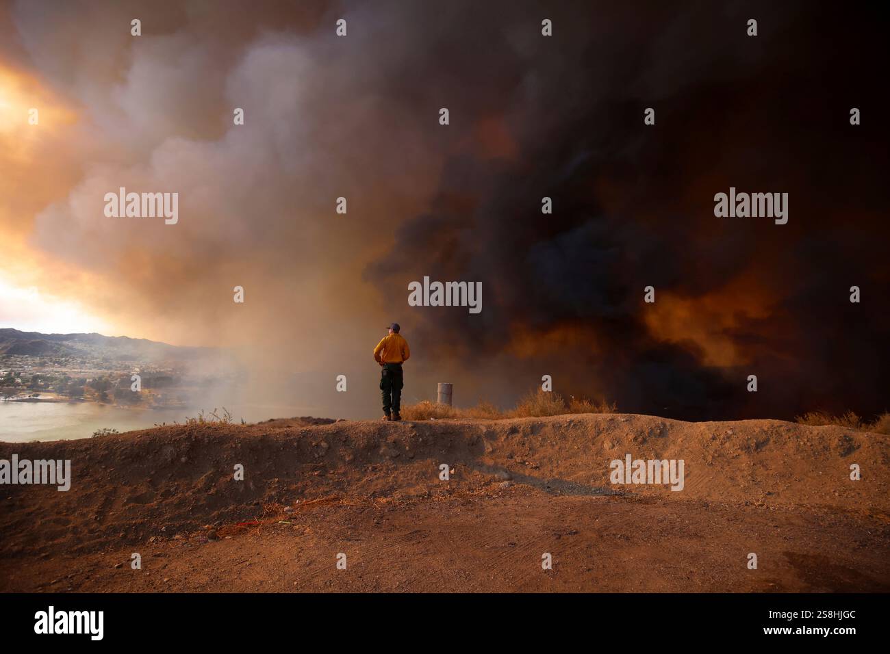 A firefighter looking out towards Lake Castaic stands on a mound ...