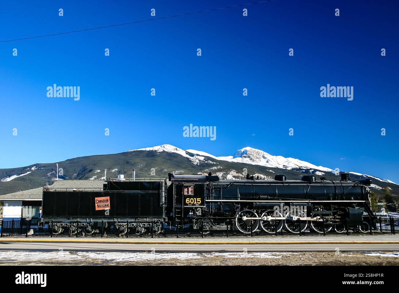 A black train is sitting on the tracks in front of a mountain. The sky ...