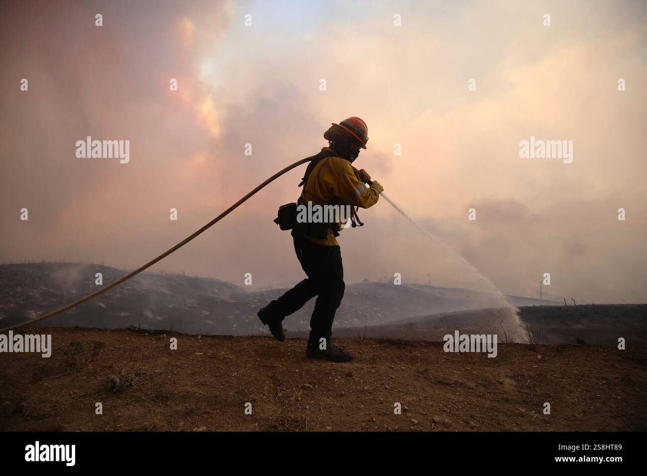 A firefighter sprays water on the ground while battling the Hughes Fire ...