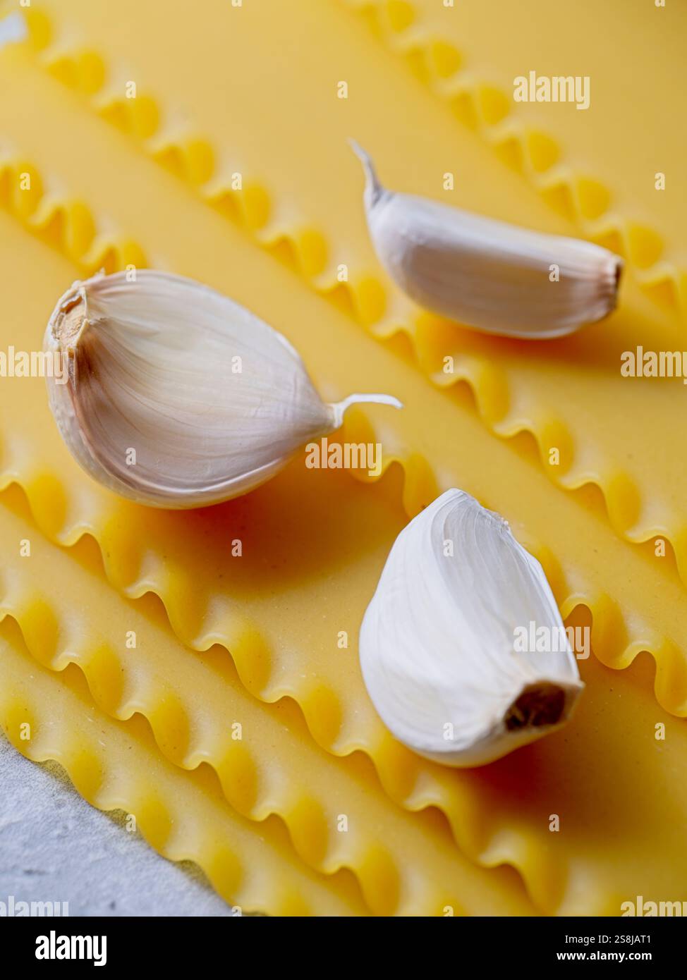 A closeup studio photo of three cloves of garlic and dried lasagna ...