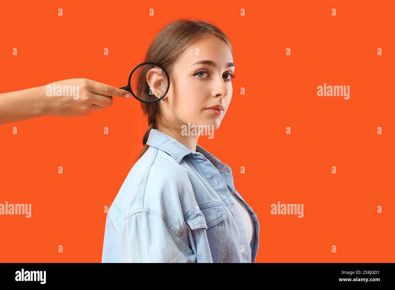 Woman magnifying teenage girl's ear with hearing aid on orange ...