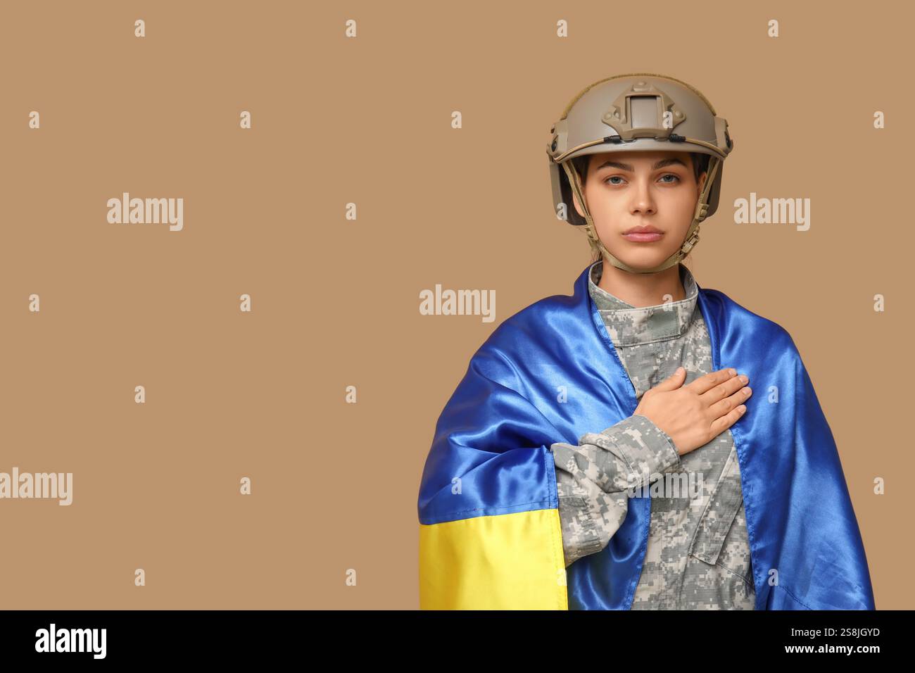 Young female soldier in uniform with flag of Ukraine on beige ...