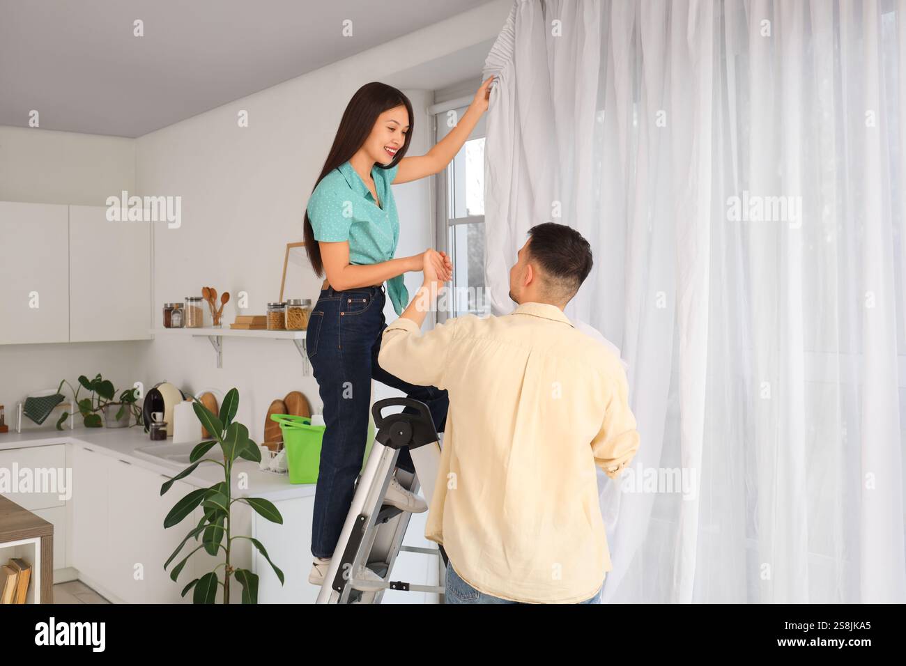 Cute young couple removing curtains from curtain track in kitchen ...