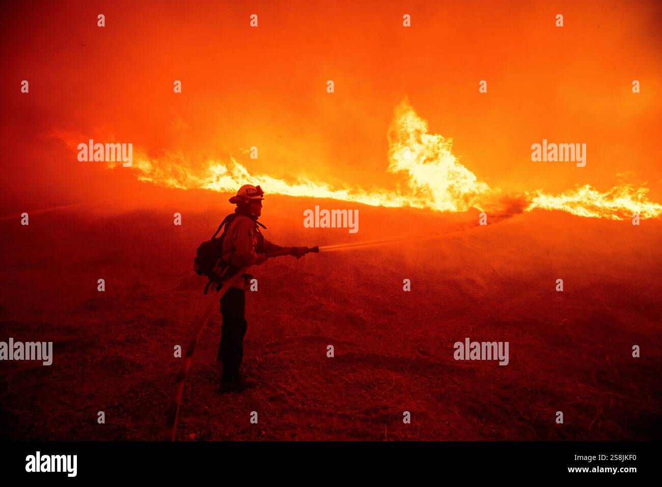 A firefighter spray water as he monitors flames caused by the Hughes ...