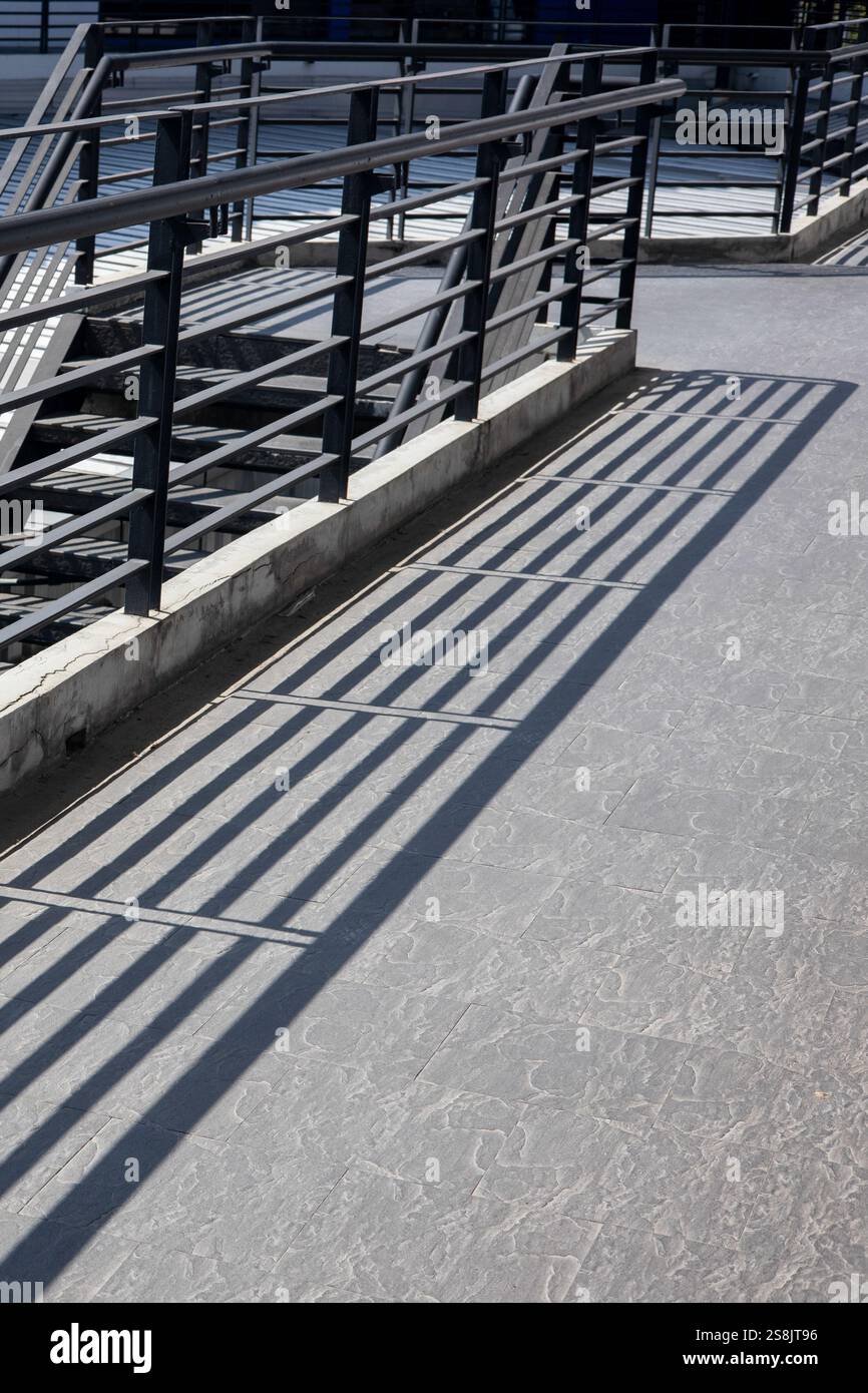 A modern black metal railing and black metal ladder, with a long shadow ...