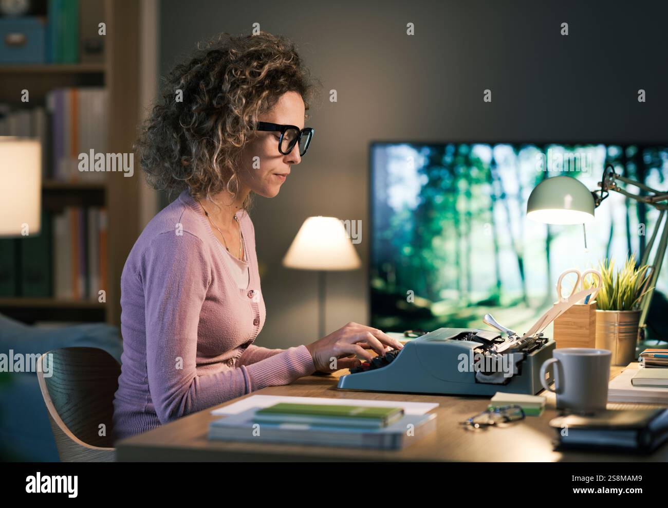 Woman sitting at her desk and typing on a vintage typewriter ...