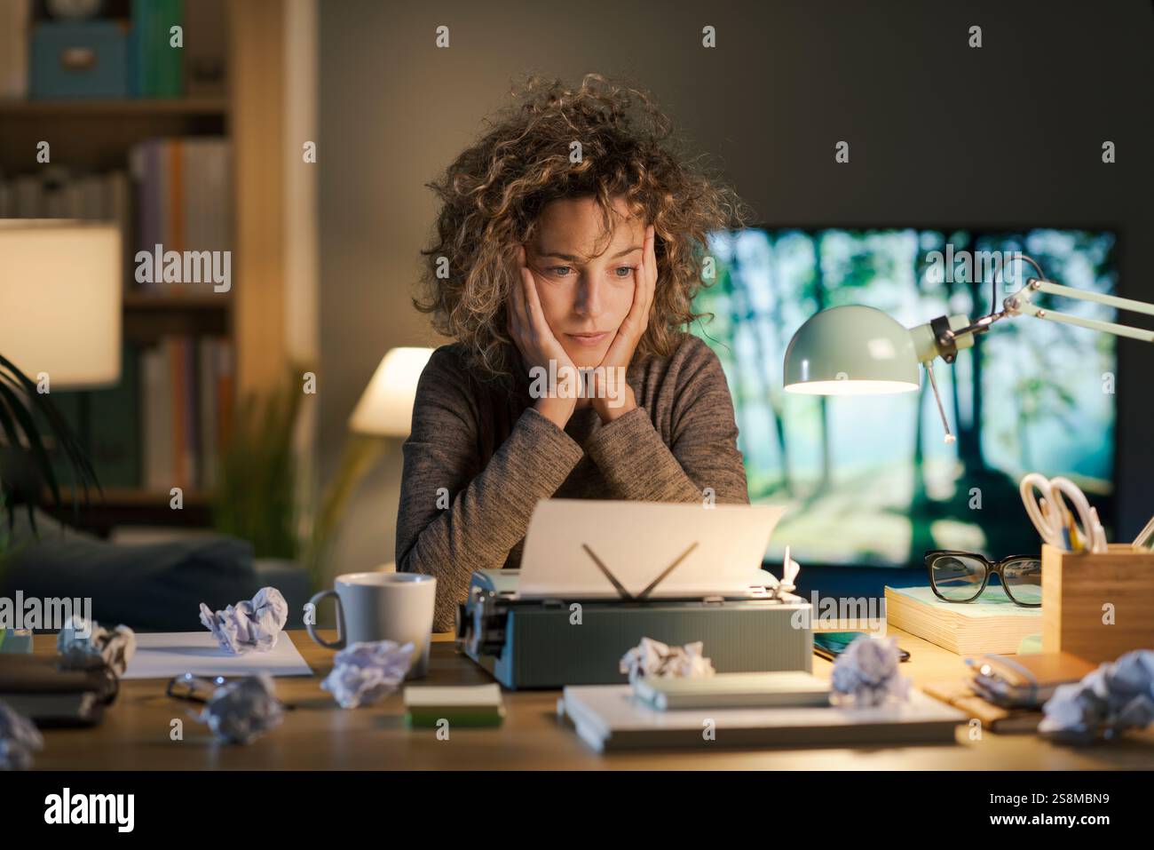 Frustrated young writer sitting at her desk with head in hands and ...