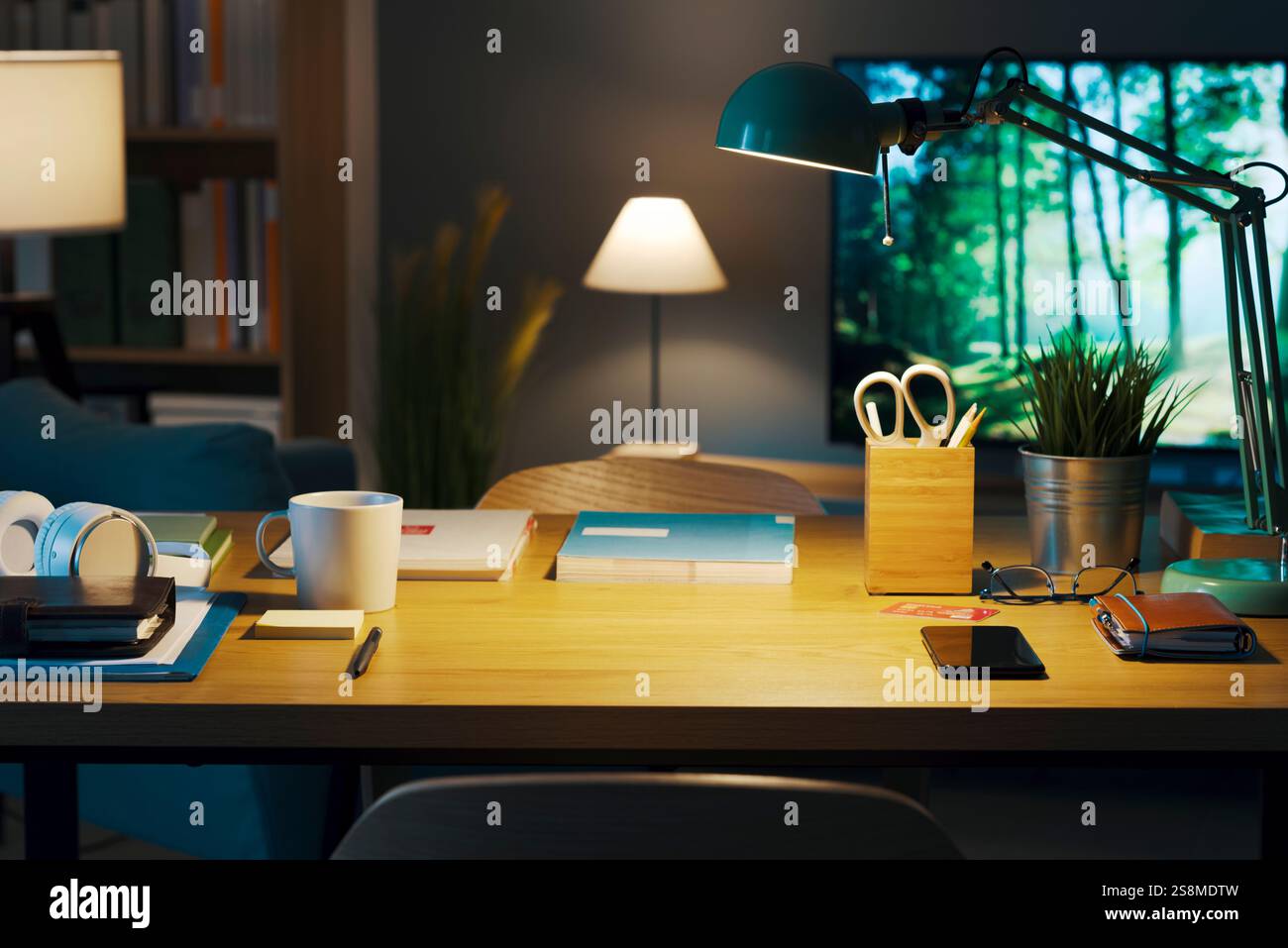 Home office interior with personal items on a tidy desk and lit lamp ...