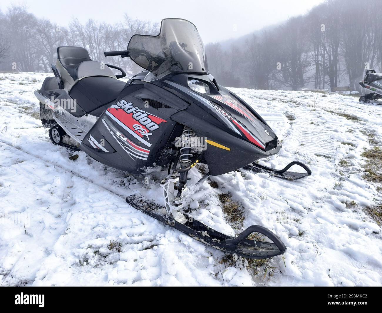 Black and red snowmobile on snowy landscape with trees in background ...