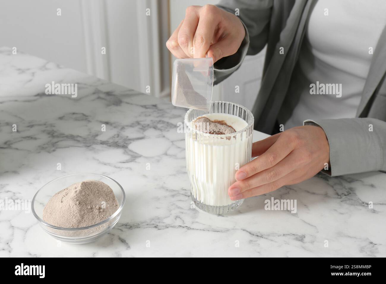Making protein cocktail. Woman adding powder into glass with milk at ...