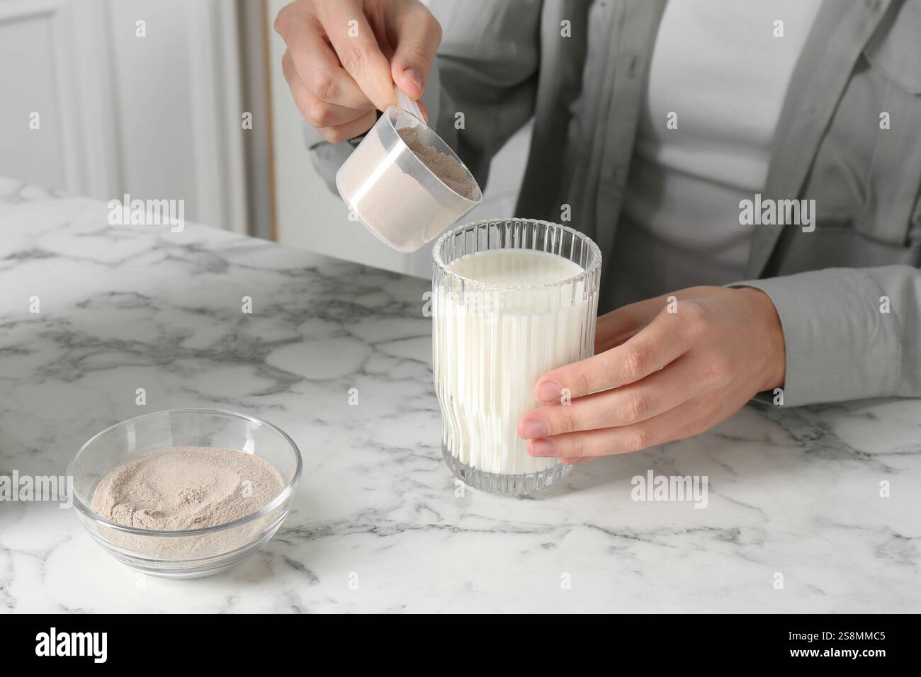 Making protein cocktail. Woman adding powder into glass with milk at ...