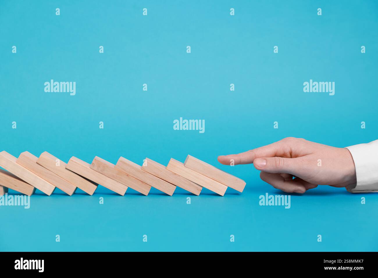 Domino effect. Woman pushing wooden blocks on light blue background ...