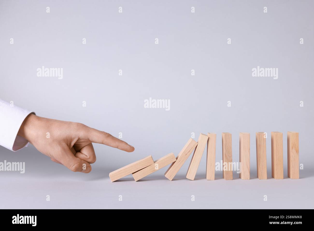Domino effect. Man pushing wooden blocks on light background, closeup ...