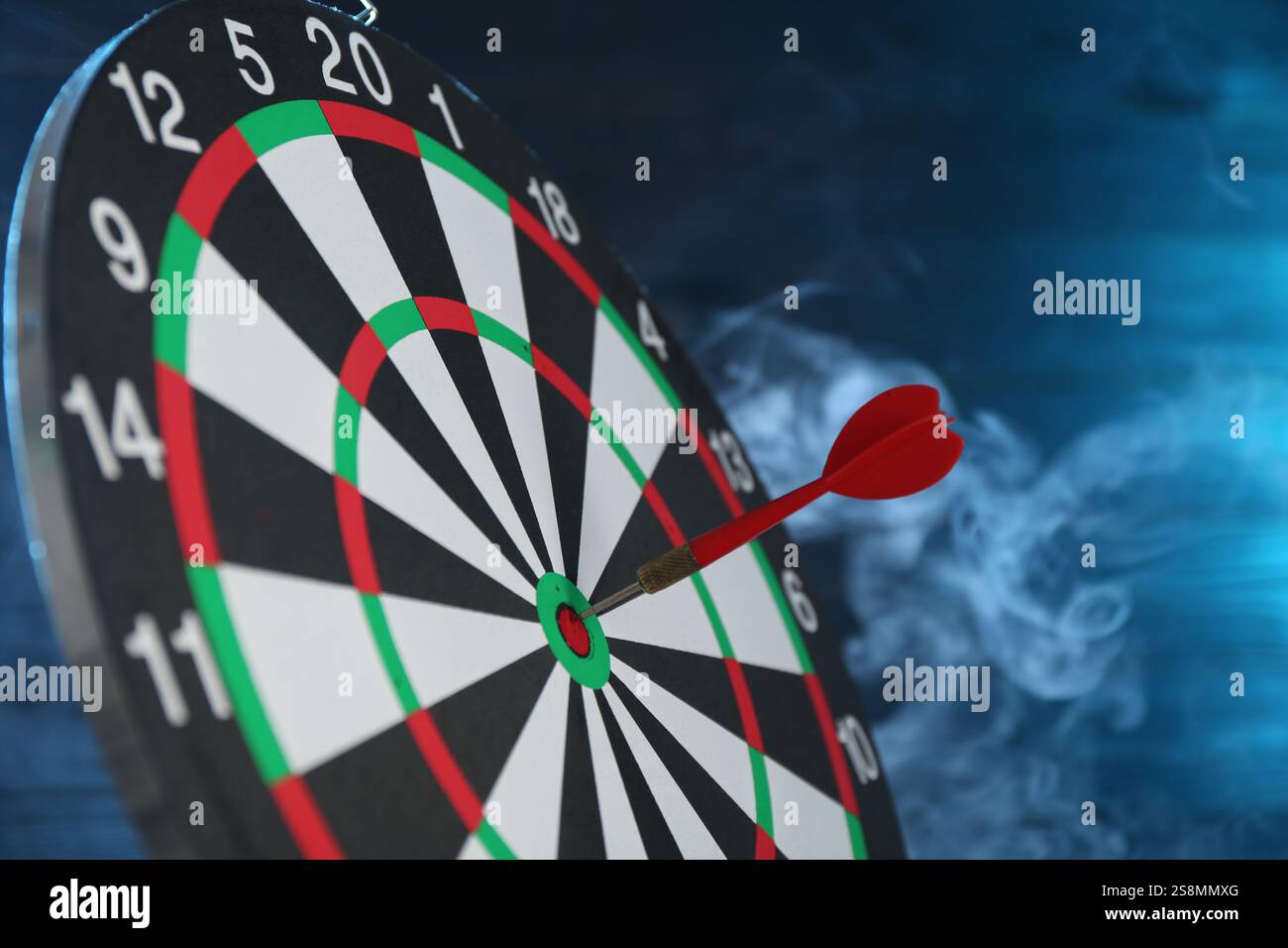Dart board with red arrow against blurred blue background in smoke ...