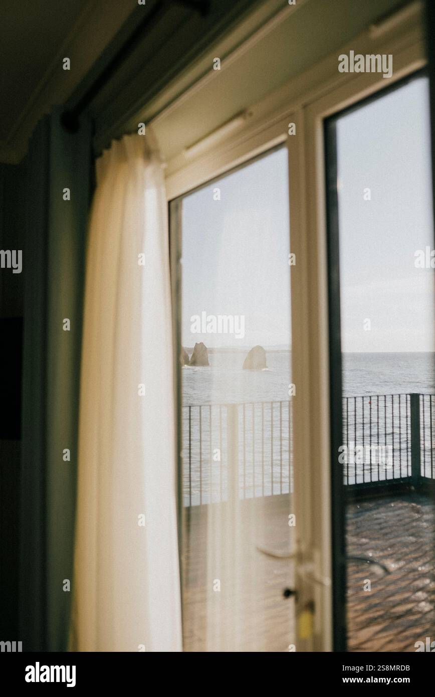 A window with a white curtain and a view of the ocean. The curtain is ...