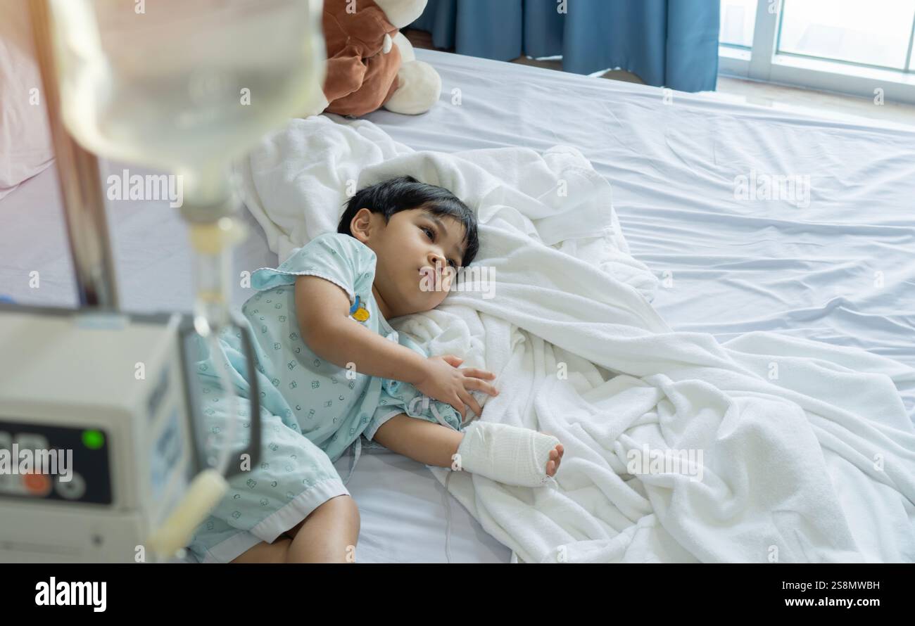 Asian little child boy patient lying down on bed and hand still lock ...