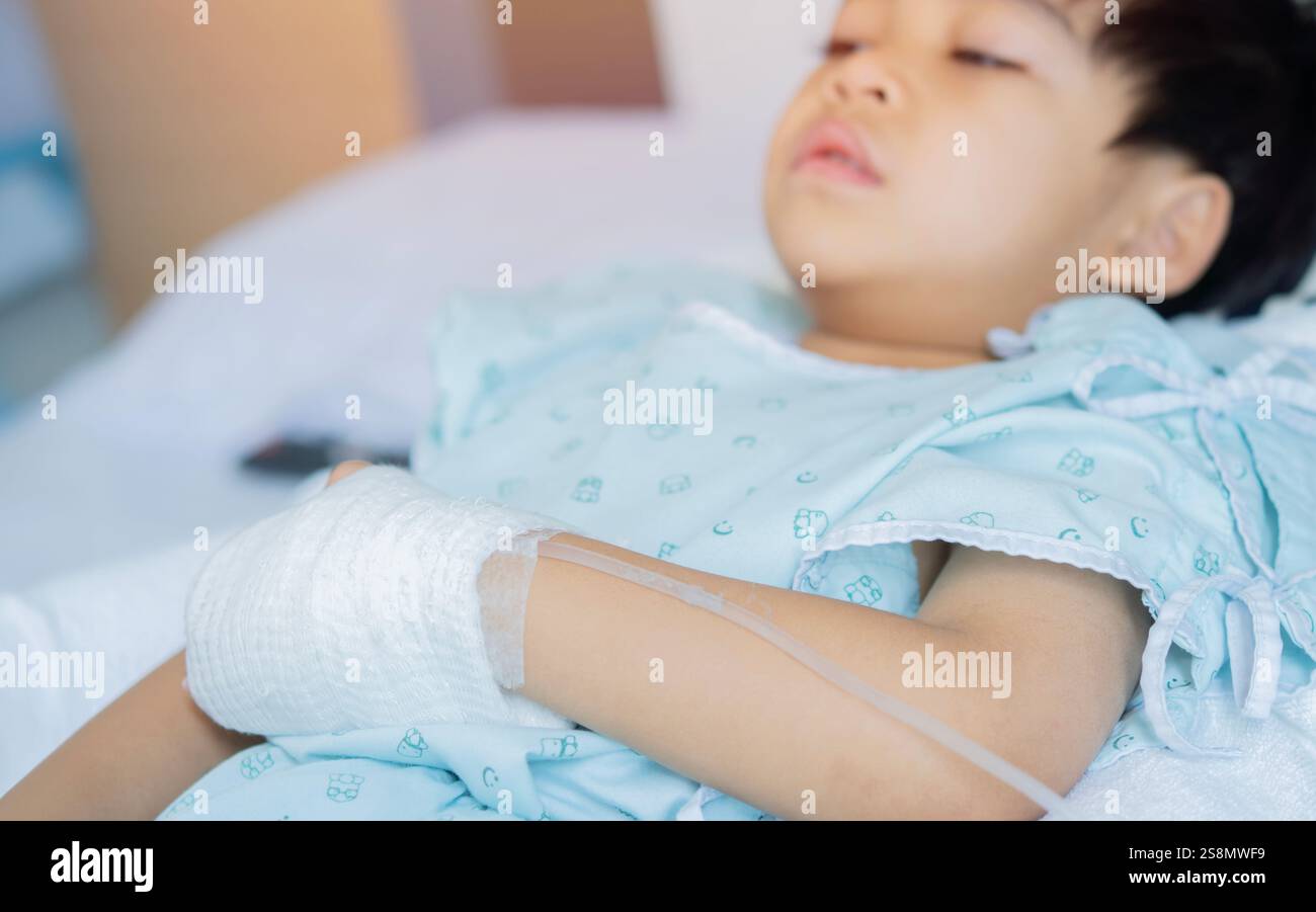 Saline line in the hand of a sick Asian boy lying in a hospital bed ...