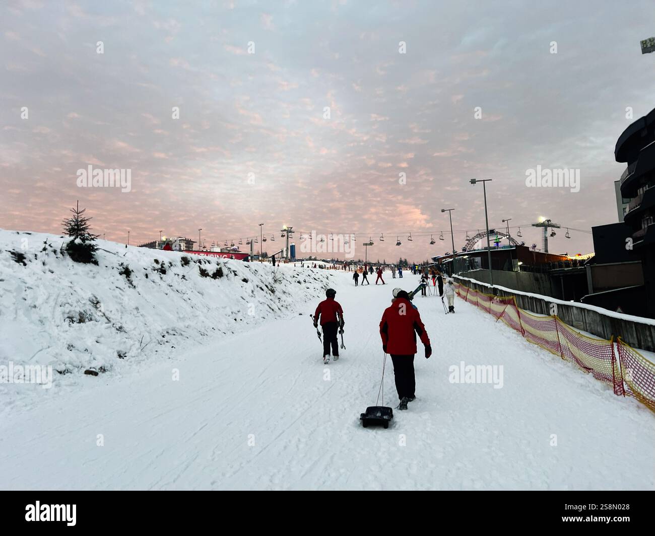 Skiiers traverse the snowy slope under a colorful sunset as others ...